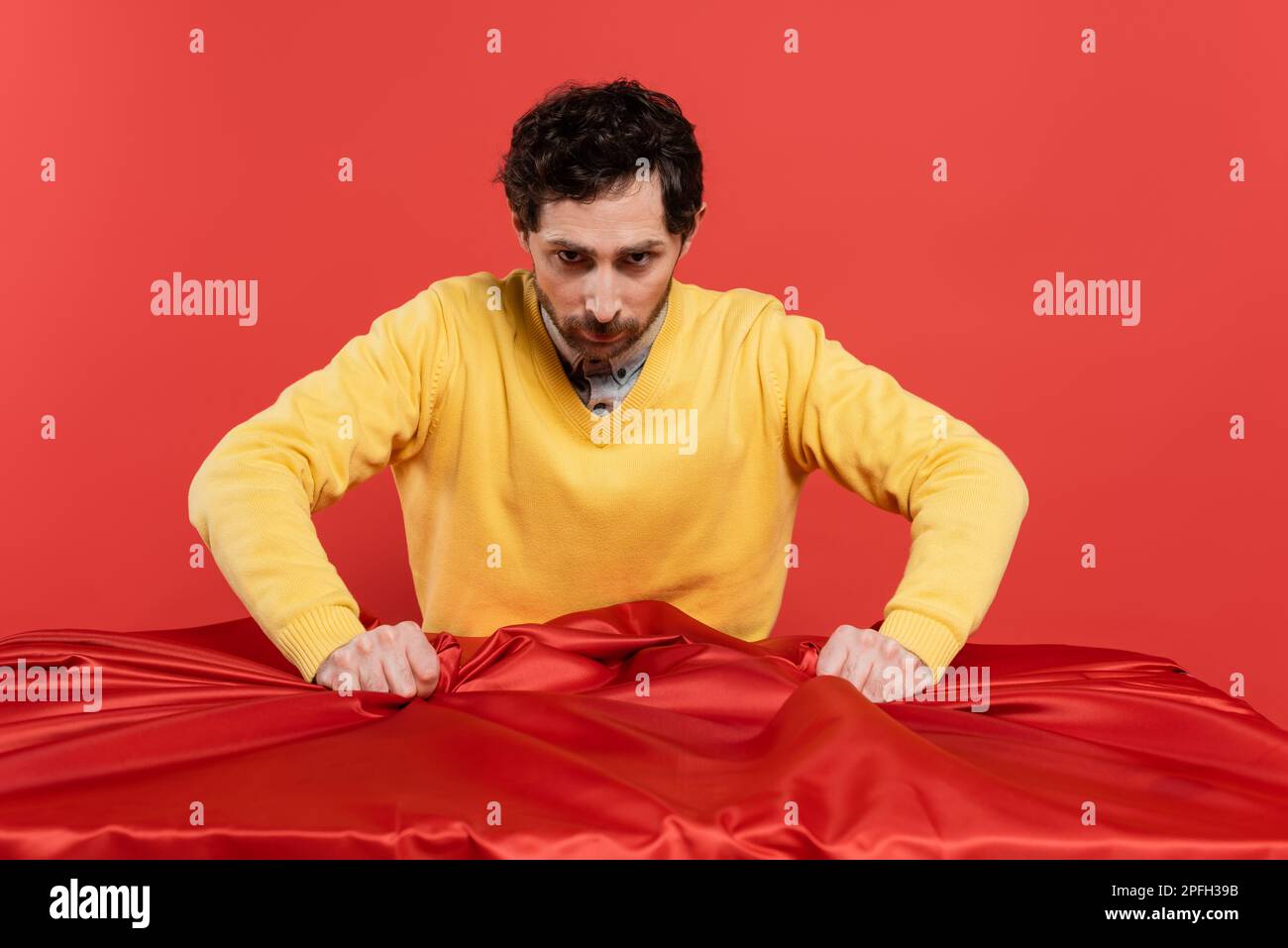 stressed man in yellow jumper pulling red tablecloth on desk isolated ...