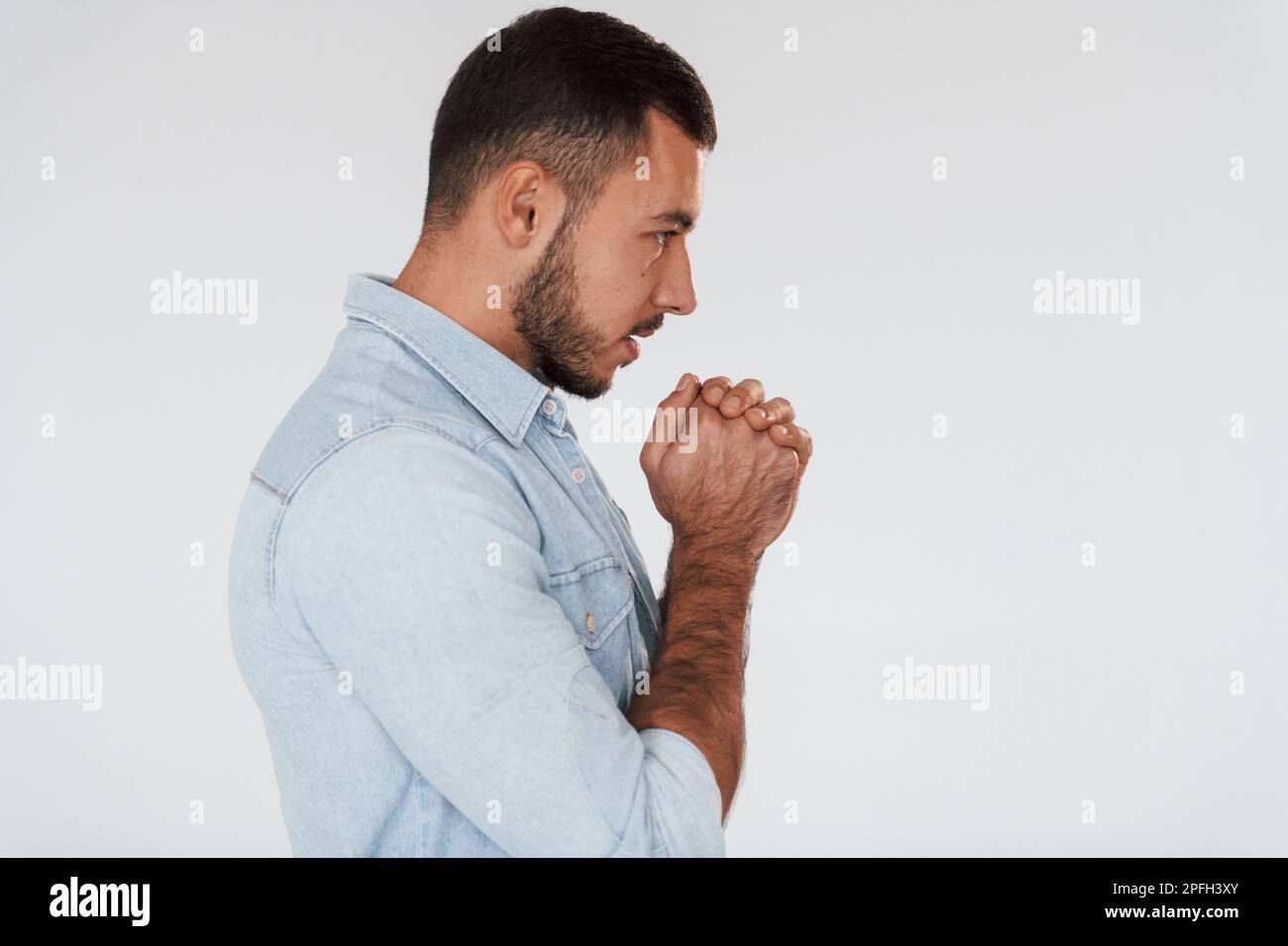 Guy is praying. Young handsome man standing indoors against white ...