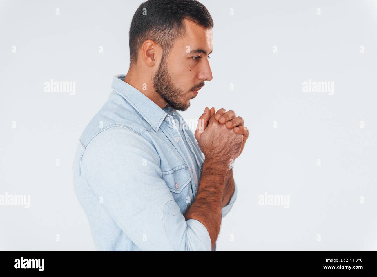 Guy is praying. Young handsome man standing indoors against white ...
