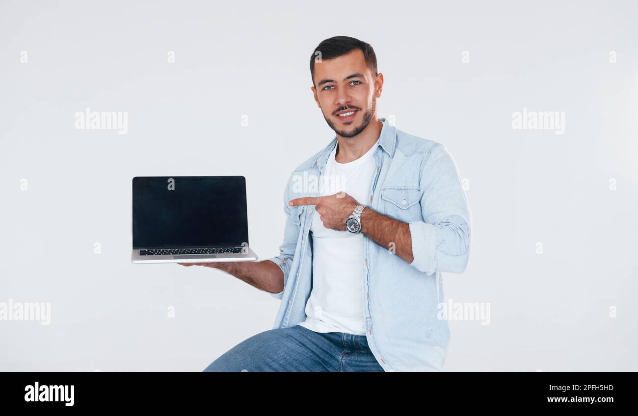 Uses laptop. Young handsome man standing indoors against white ...