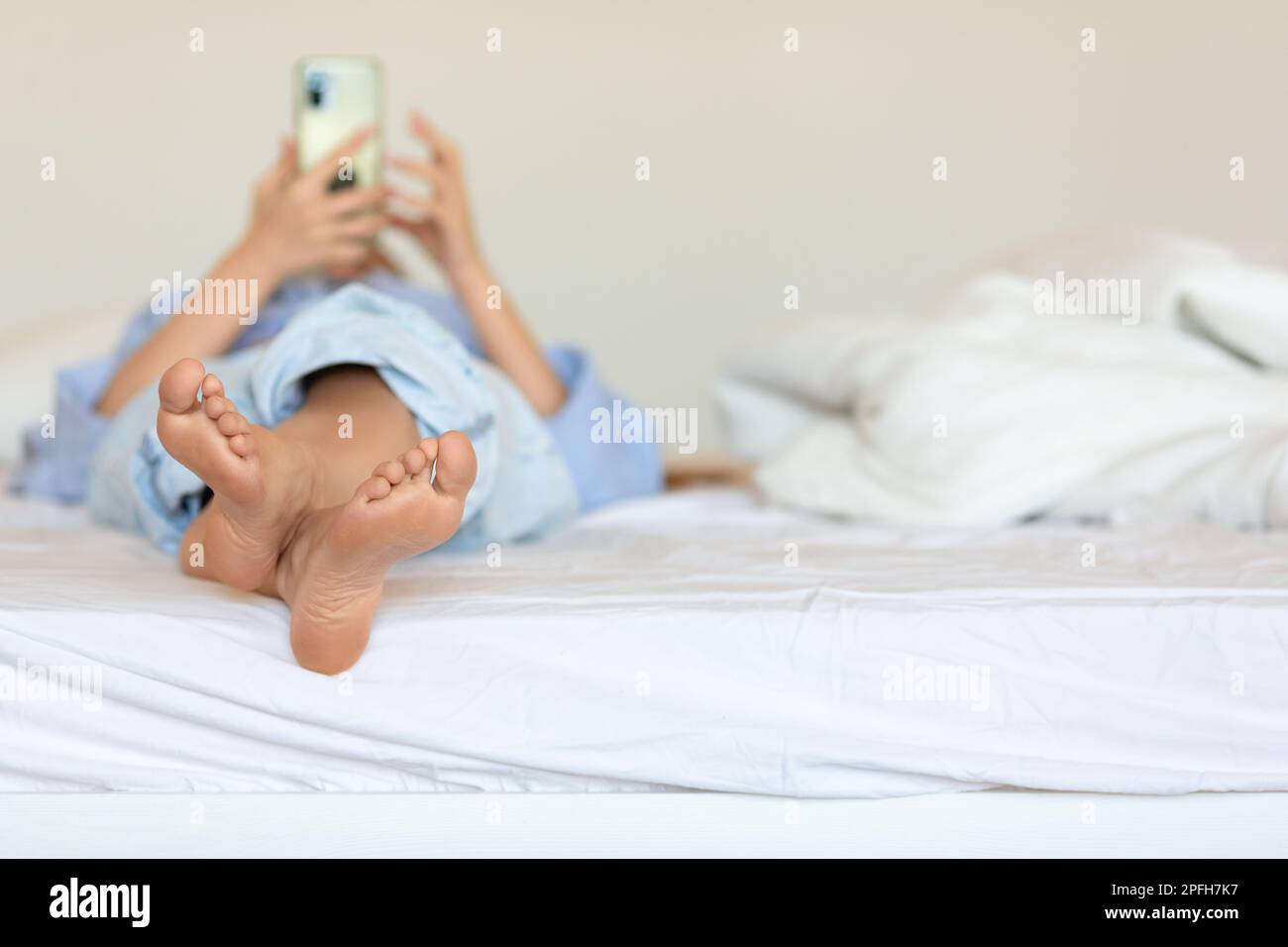 Woman lying on her bed with her legs facing the camera, absorbed in ...