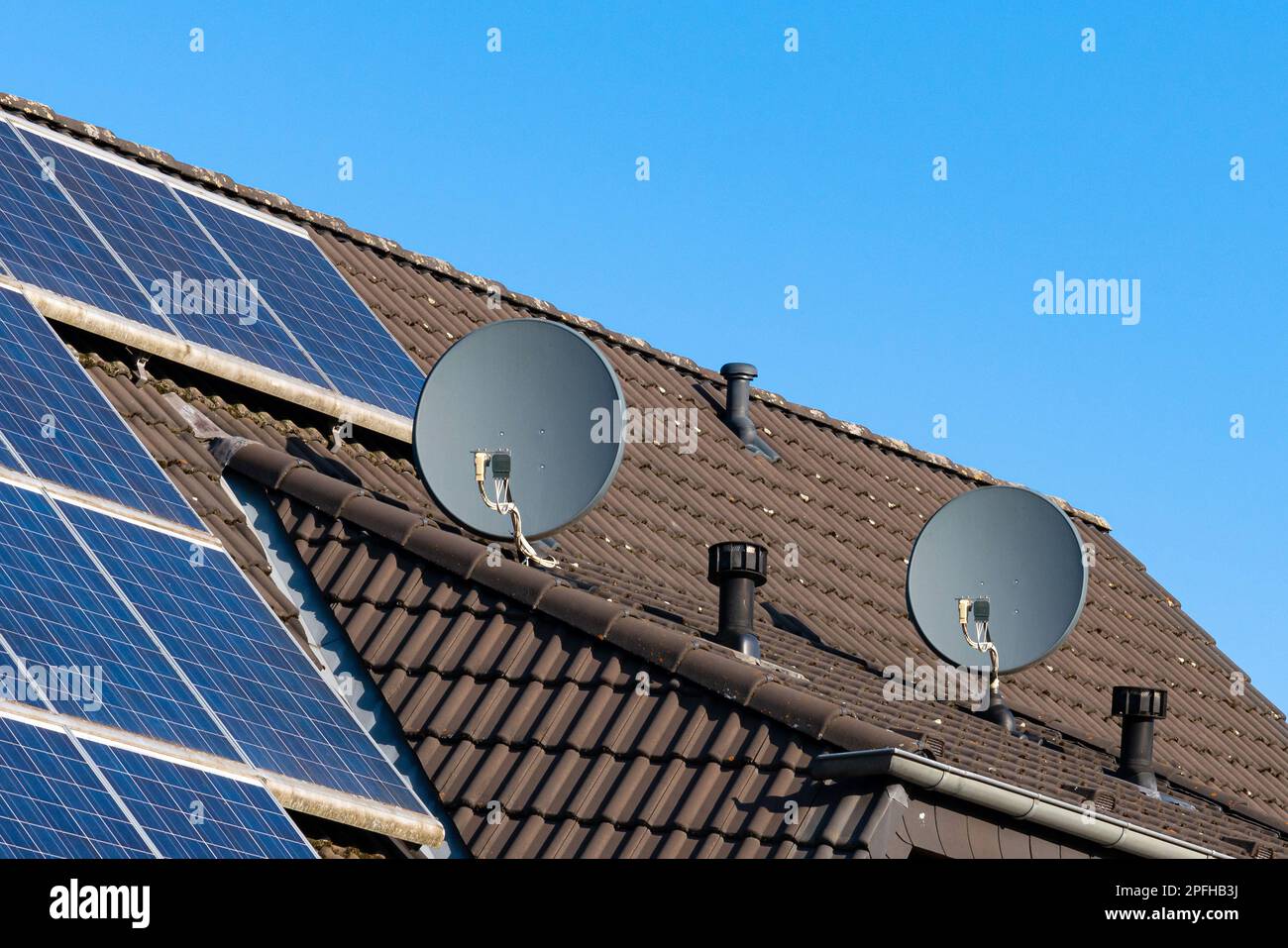 Two satellite dishes on the roof of a tiled house. Solar panels on the ...