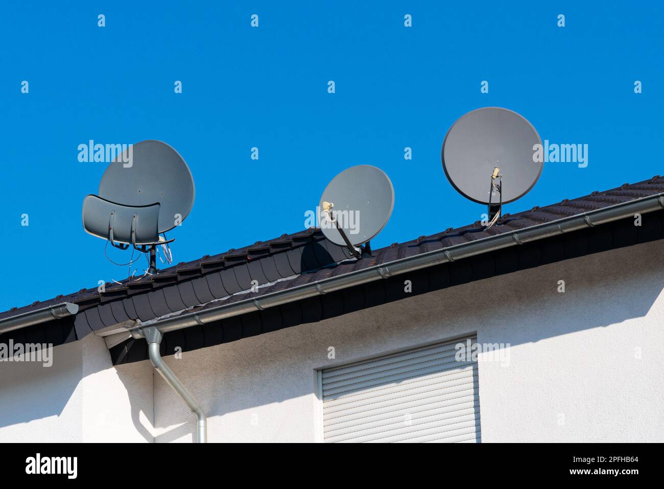 Three satellite dishes on the roof of a tiled house. Clear blue sky ...