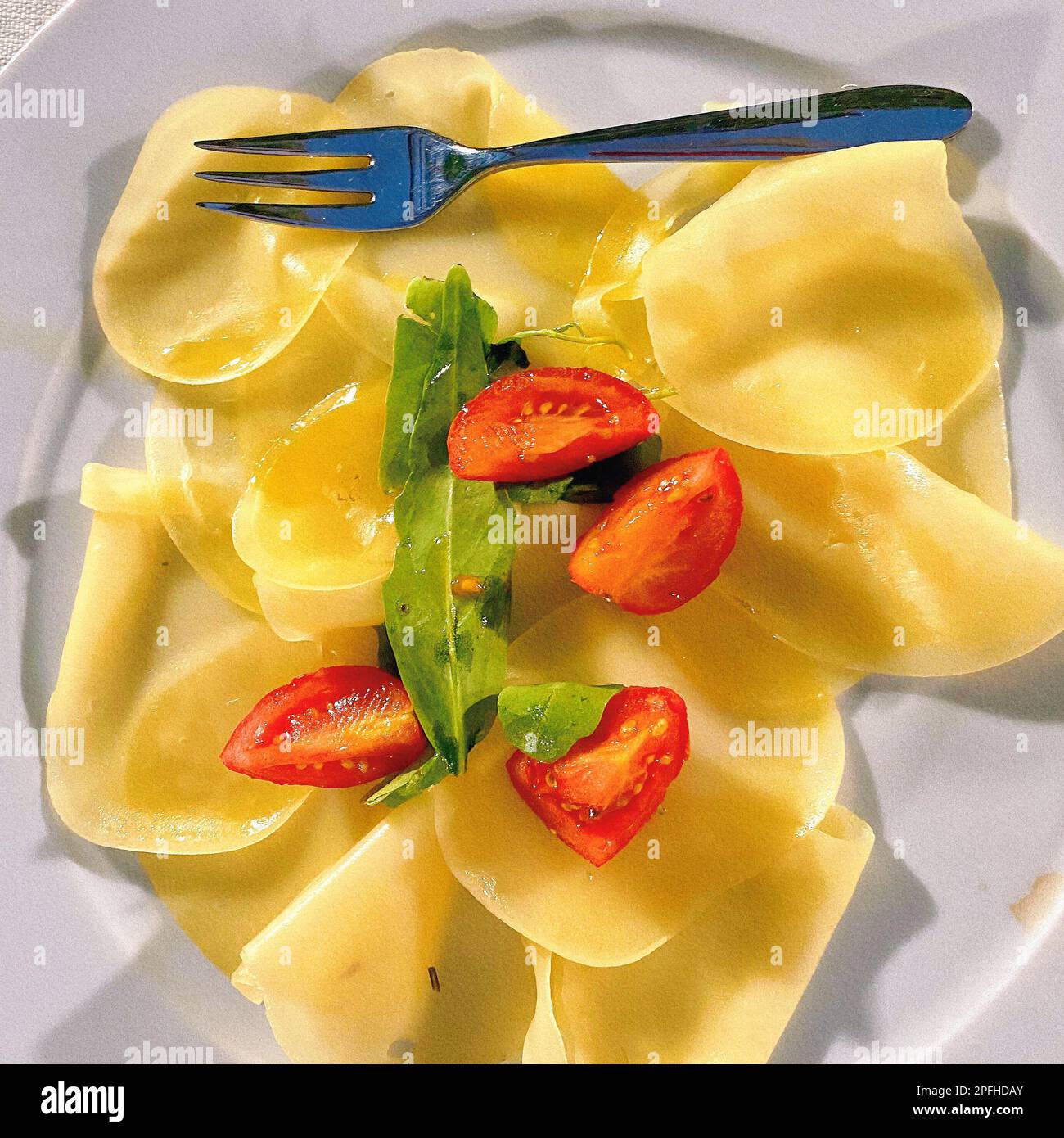 A white plate with ravioli pasta with tomato slices and a silver fork ...