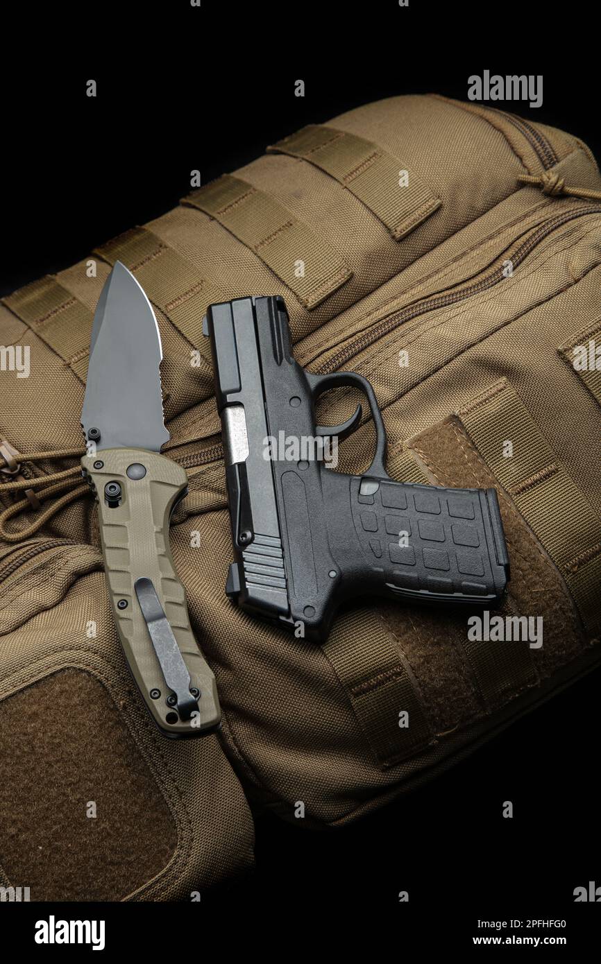 A small modern pistol and penknife on a brown military backpack. Self ...