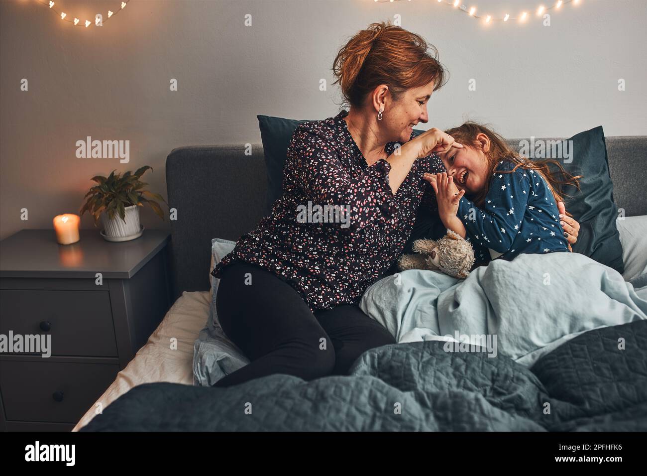Mother playing with her little daughter in bed, having fun before going ...