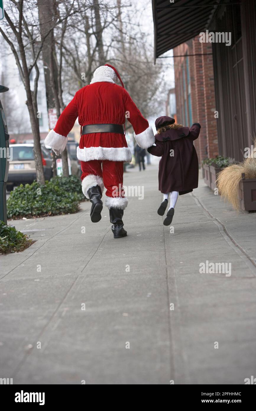 A man dressed as Santa clause walking down the street holding hands ...