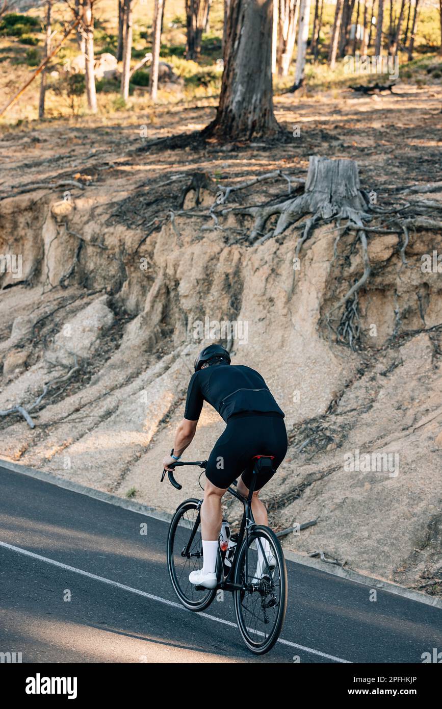 Back view of a male cyclist in black sports attire riding his bike up a ...