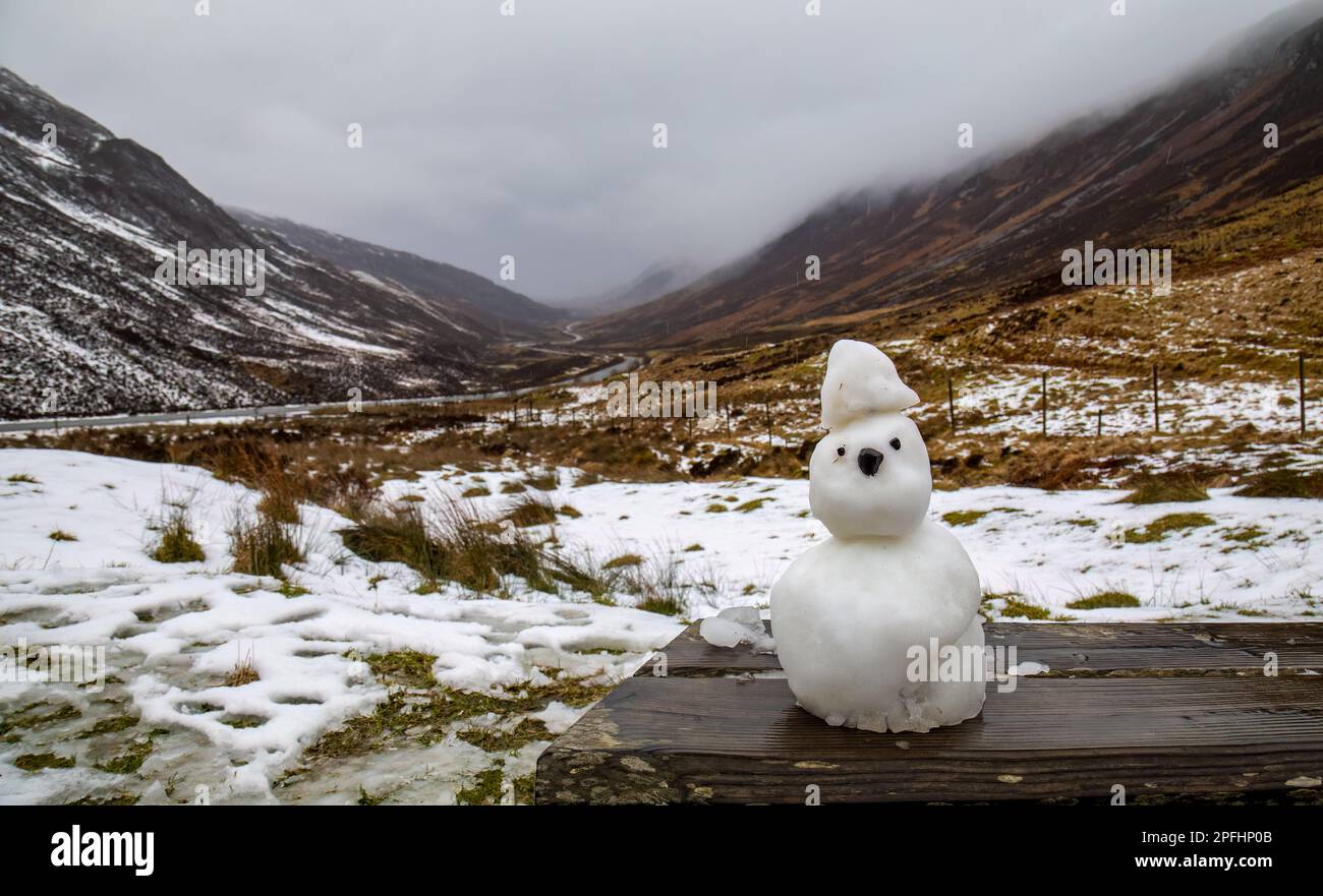 A snowman on a rustic wooden bench situated in an idyllic mountain ...