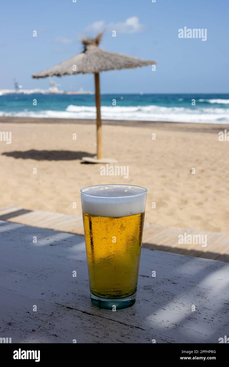 Glass of a beer in a shadow of a bar. Sun umbrella and Atlantic ocean ...