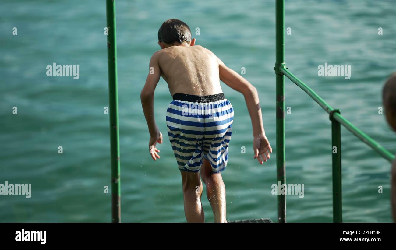 Young boy running diving into water. Teen child plunges in lake by dock ...