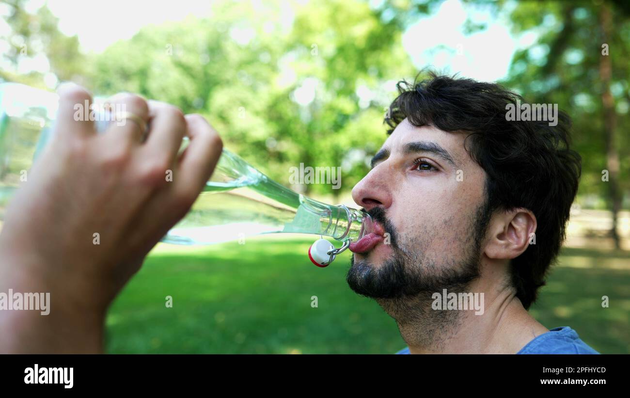 Young man consuming water to clench thirst outside during summer day at ...