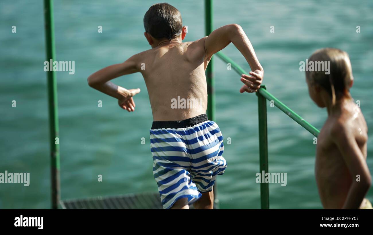 Young boy running diving into water. Teen child plunges in lake by dock ...