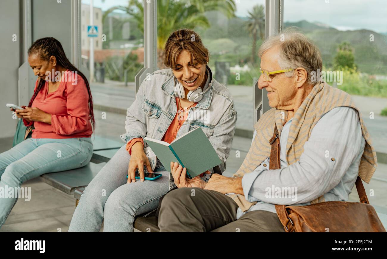 Multiracial people reading a book while waiting at tram station in the ...