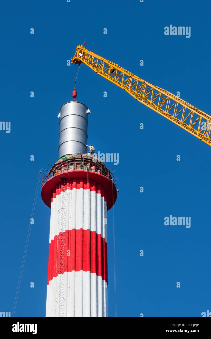 Top of tall factory chimney at renovation and crane arm on blue sky ...