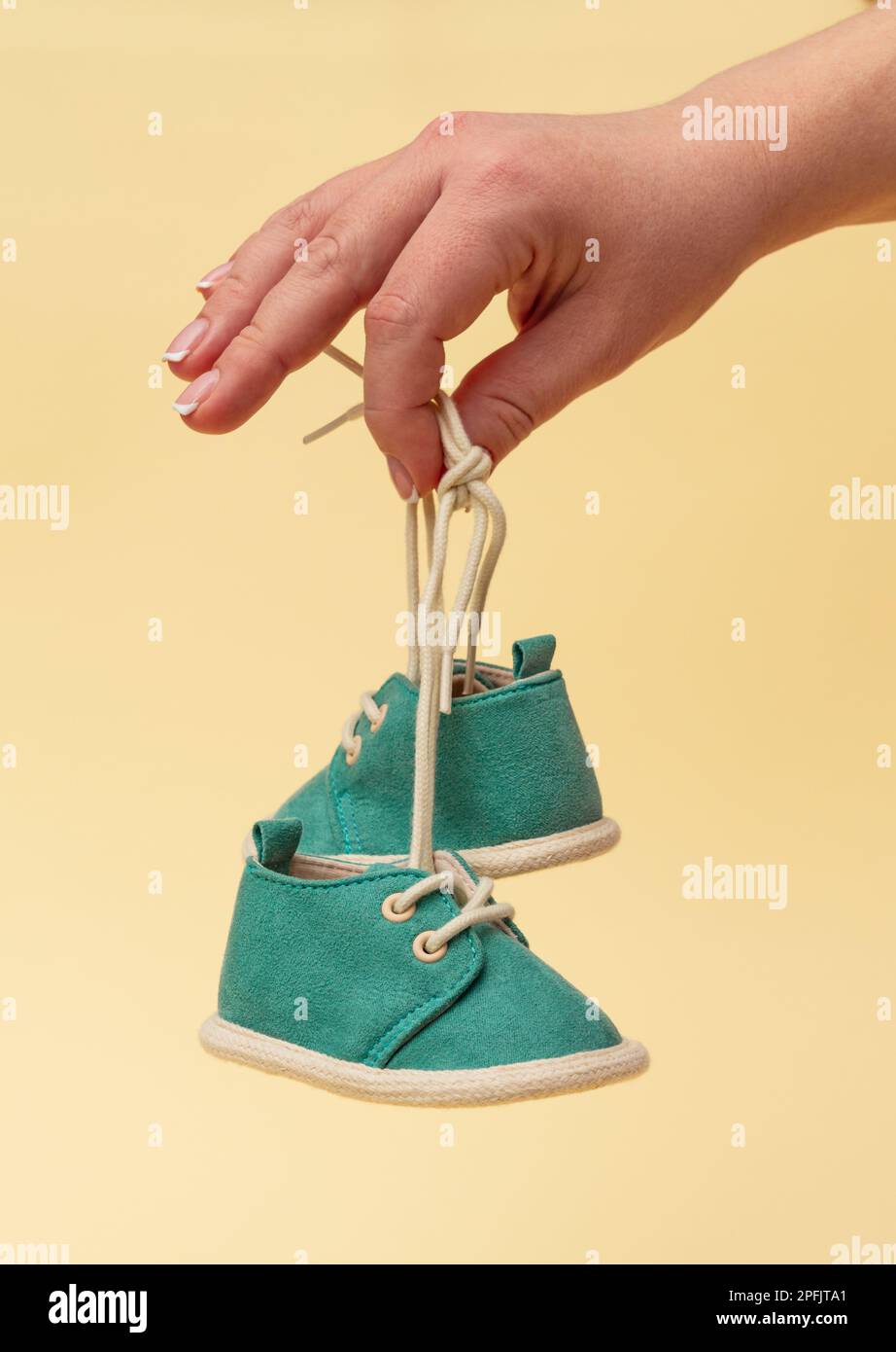 Woman holding newborn baby tiny shoes with laces on yellow background ...