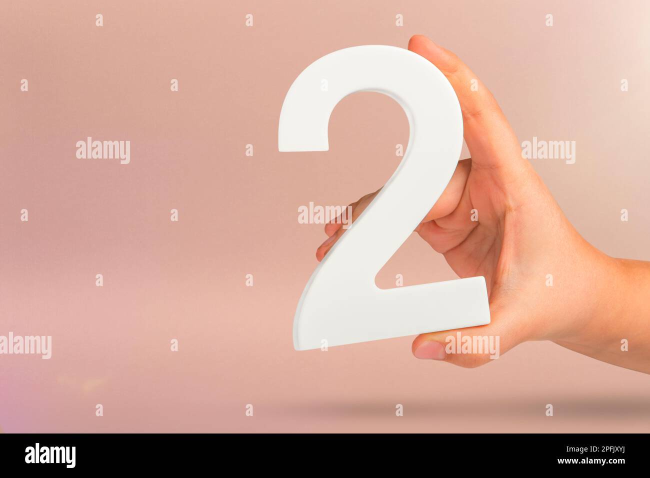 Number two in hand. Hand holding white number 2 on red background with ...
