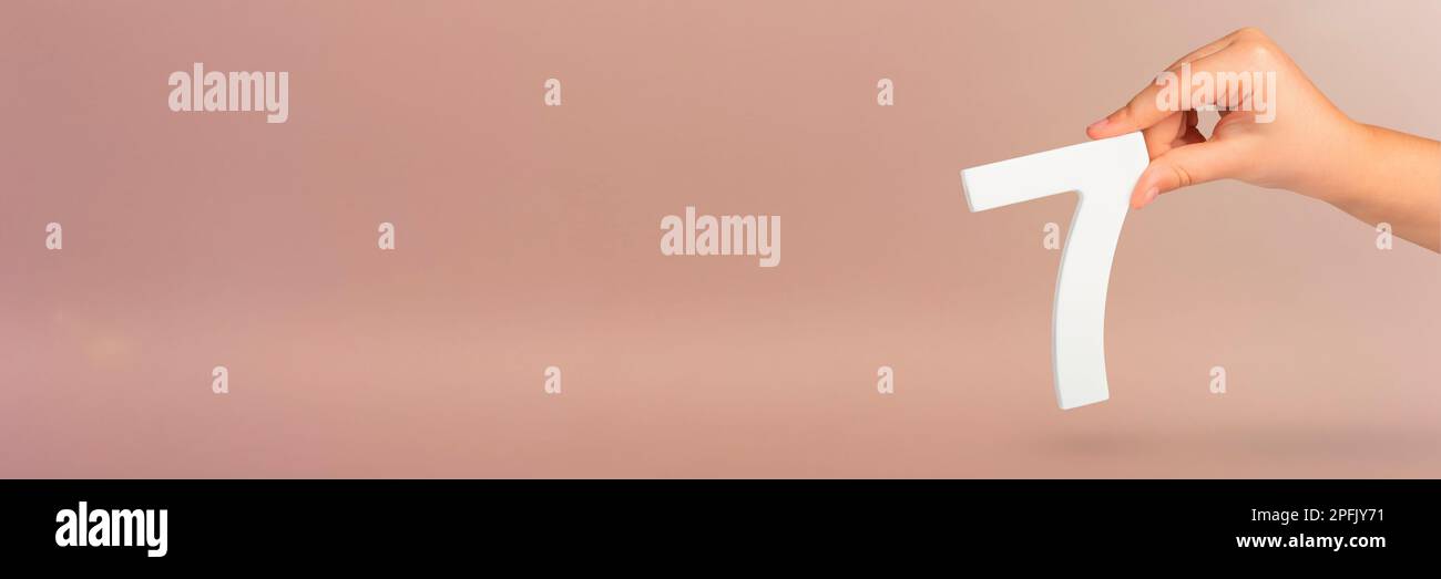 Number seven in hand. Hand holding white number 7 on red background ...
