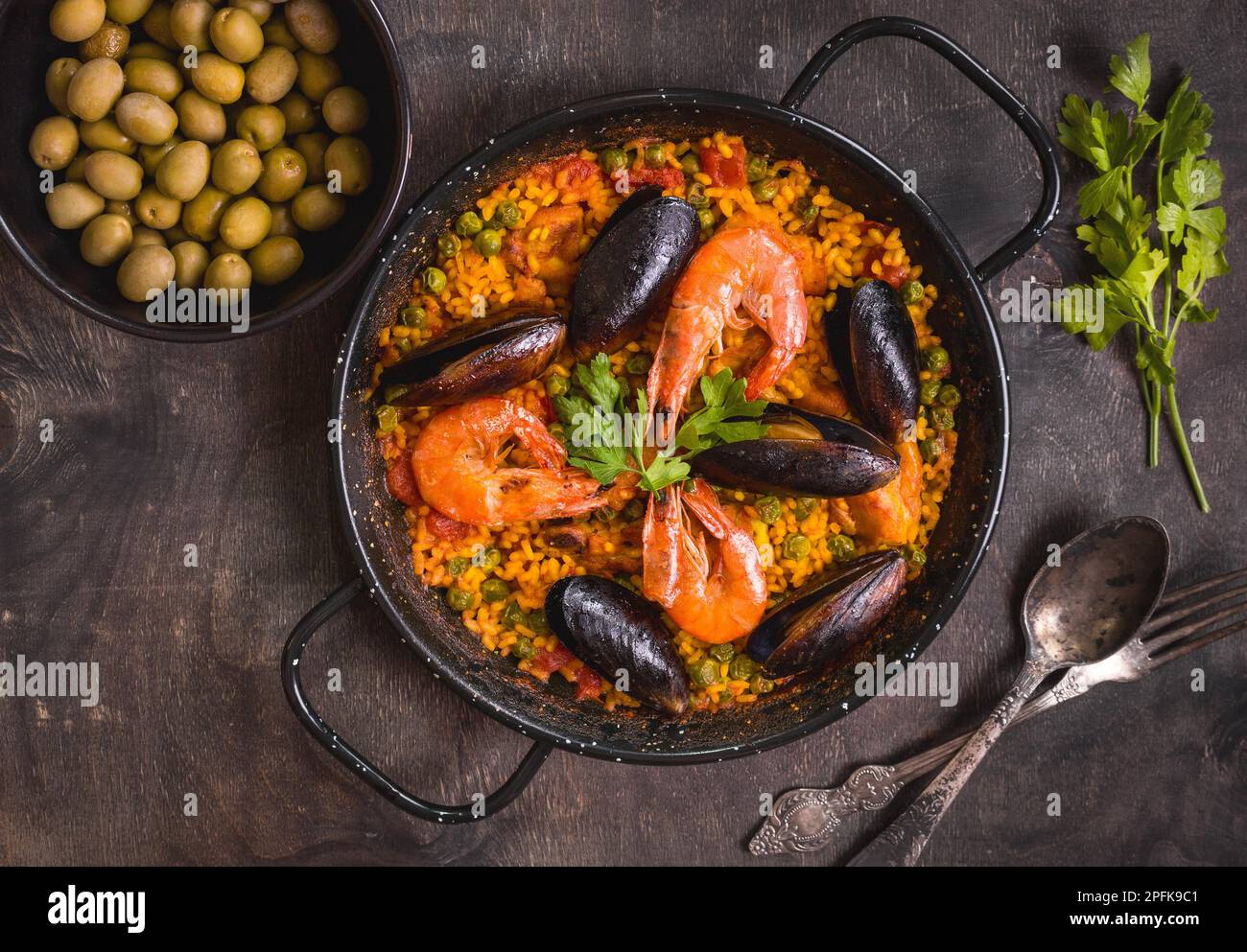 Paella in black pan with rice, shrimps, mussels, squid and meat, bowl ...