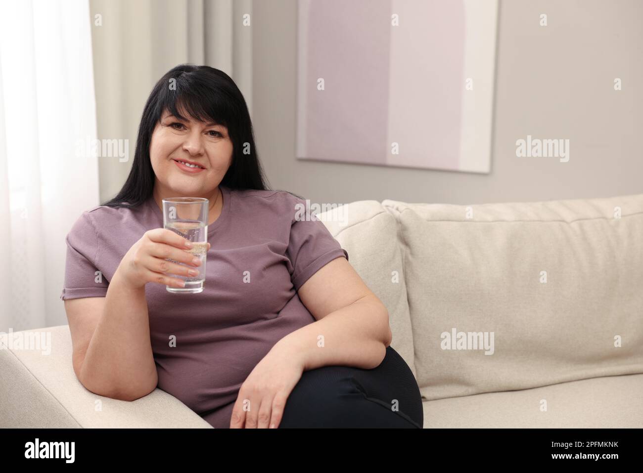 Beautiful overweight woman with glass of water on sofa at home Stock ...