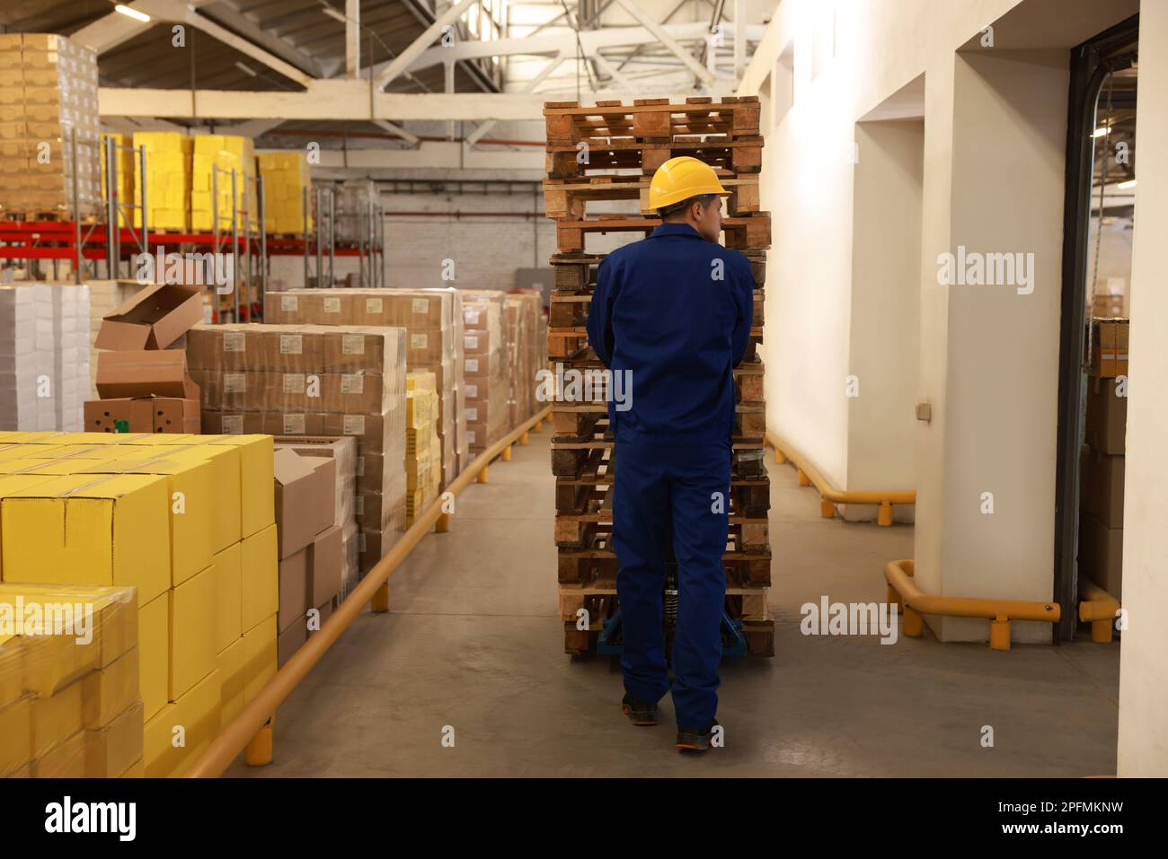 Worker moving wooden pallets with manual forklift in warehouse, back ...