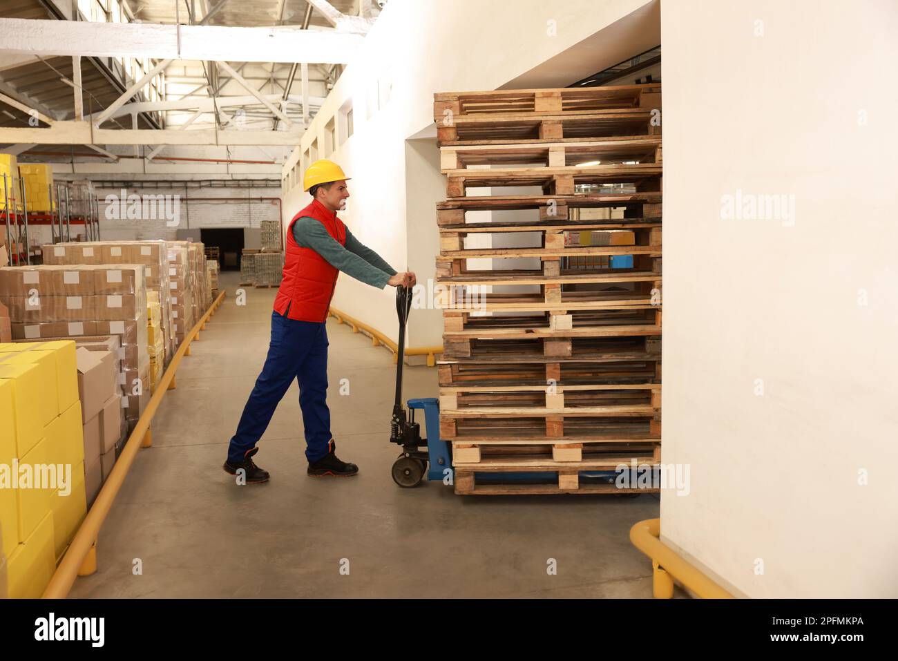 Worker moving wooden pallets with manual forklift in warehouse Stock ...