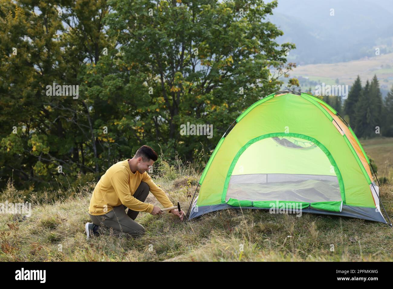 Man setting up camping tent on hill Stock Photo - Alamy