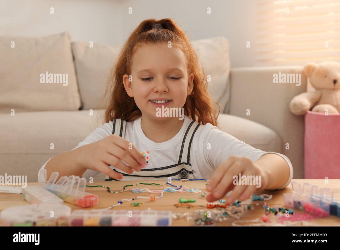 Cute girl making beaded jewelry at table in room Stock Photo - Alamy