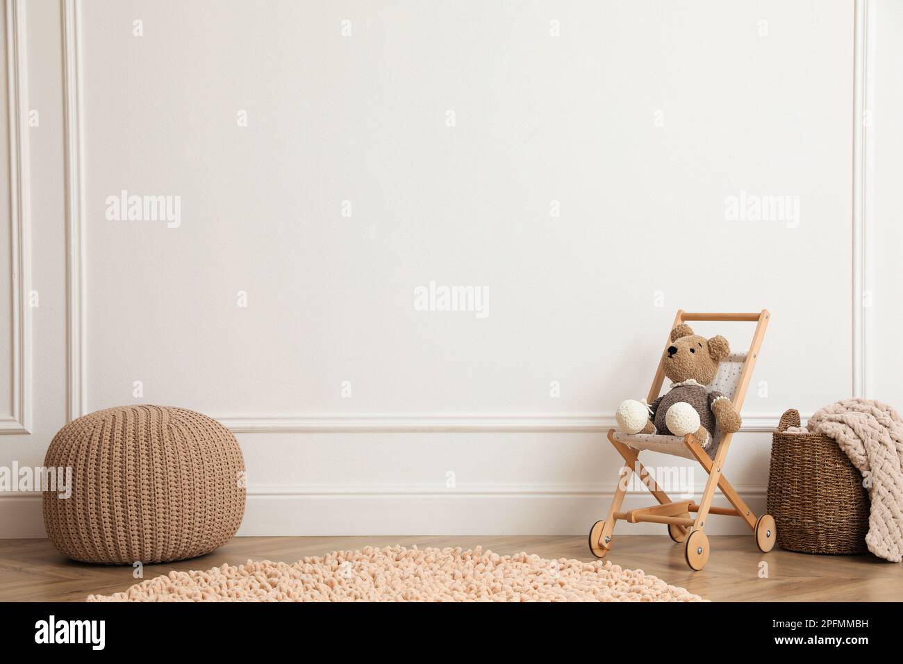 Toy stroller with bear, pouf and wicker basket near white wall in child ...
