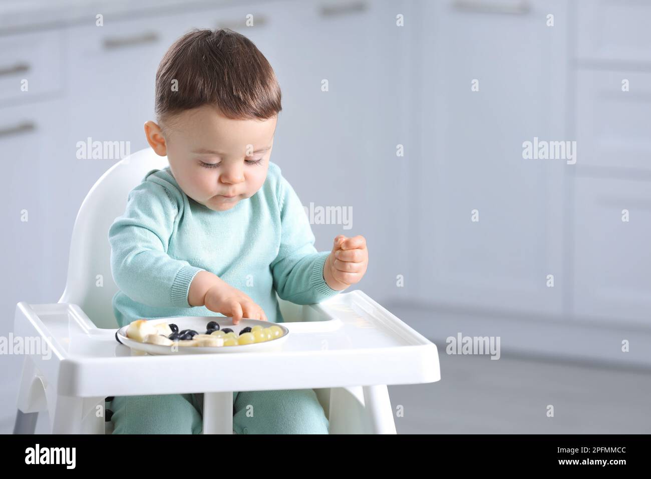 Cute little baby eating healthy food in high chair at home. Space for ...
