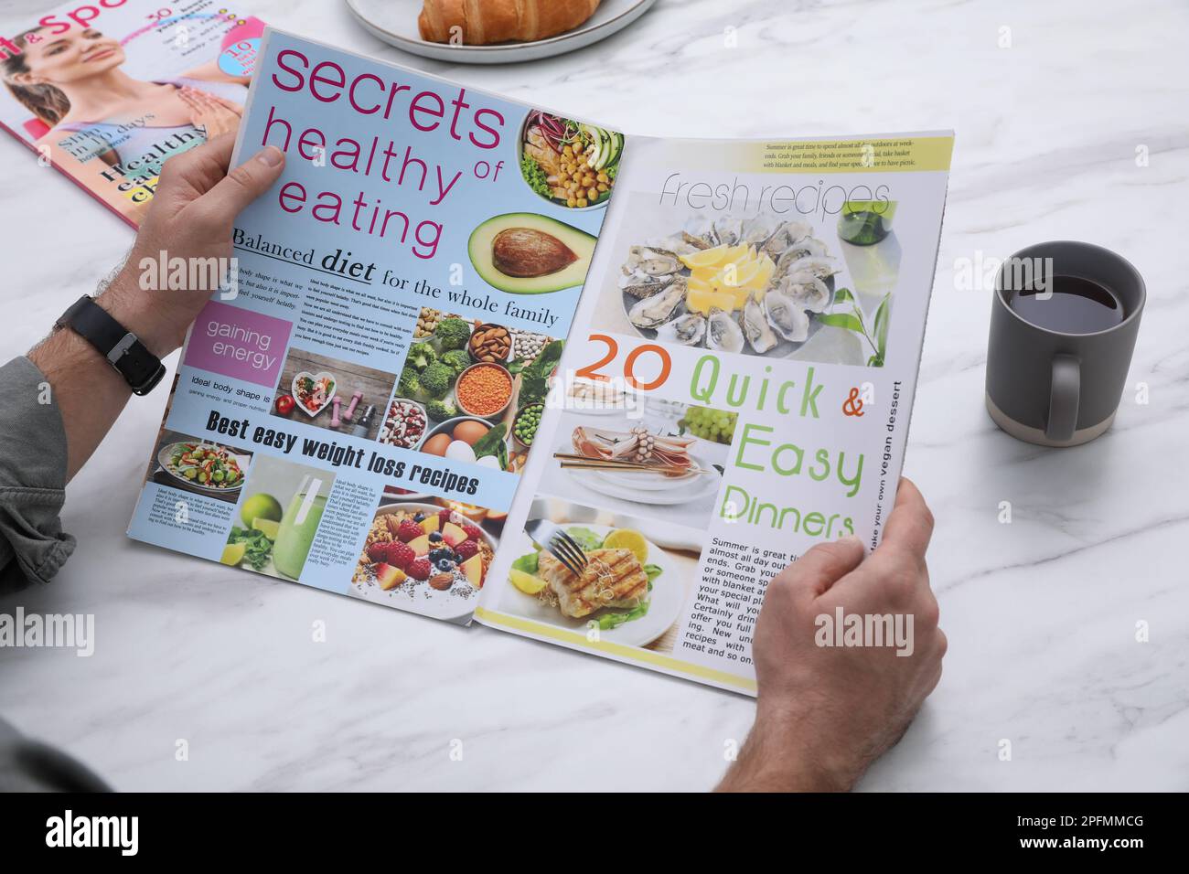Man reading magazine during breakfast at white marble table, closeup ...