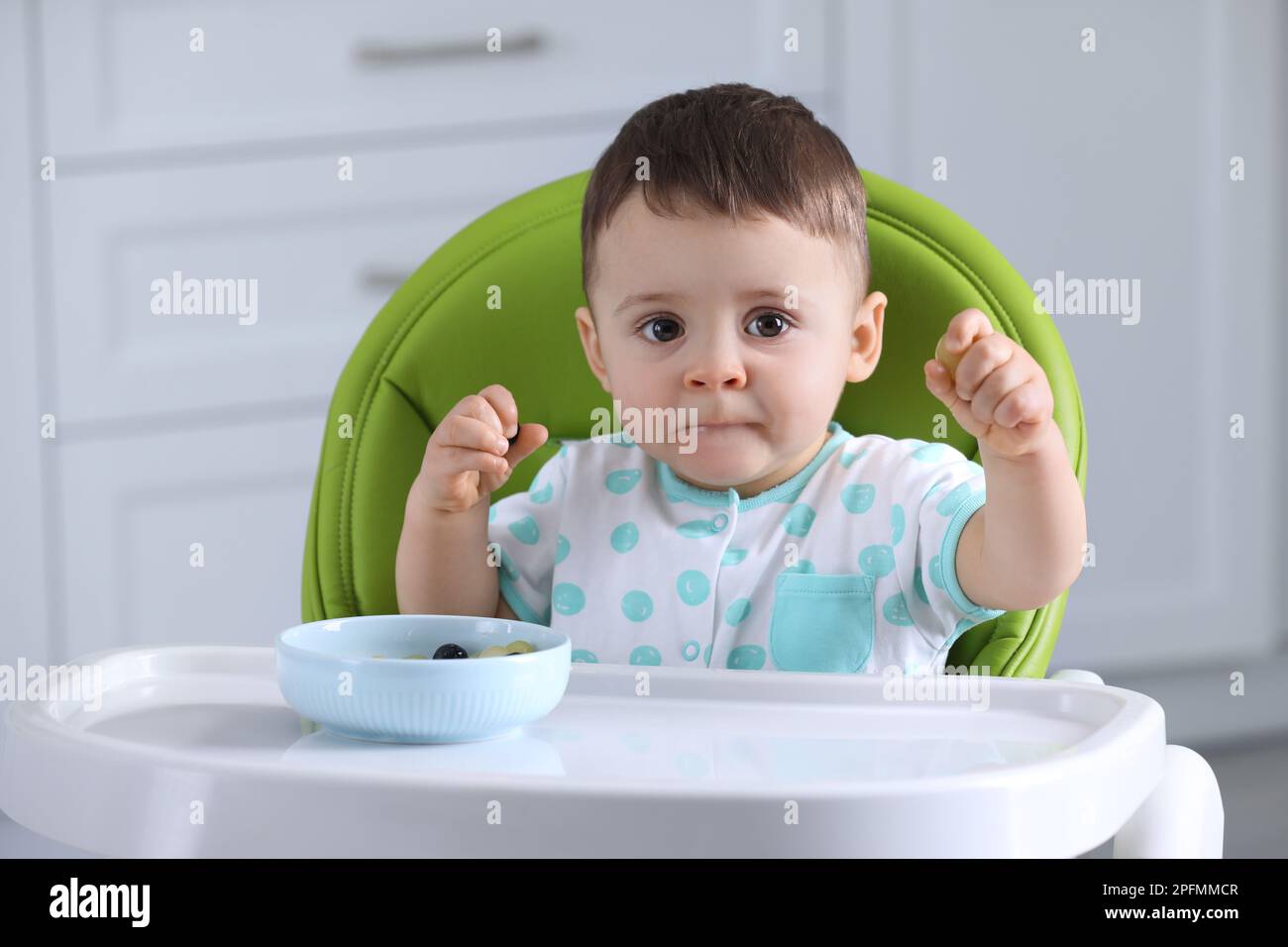 Cute little baby eating healthy food in high chair at home Stock Photo ...