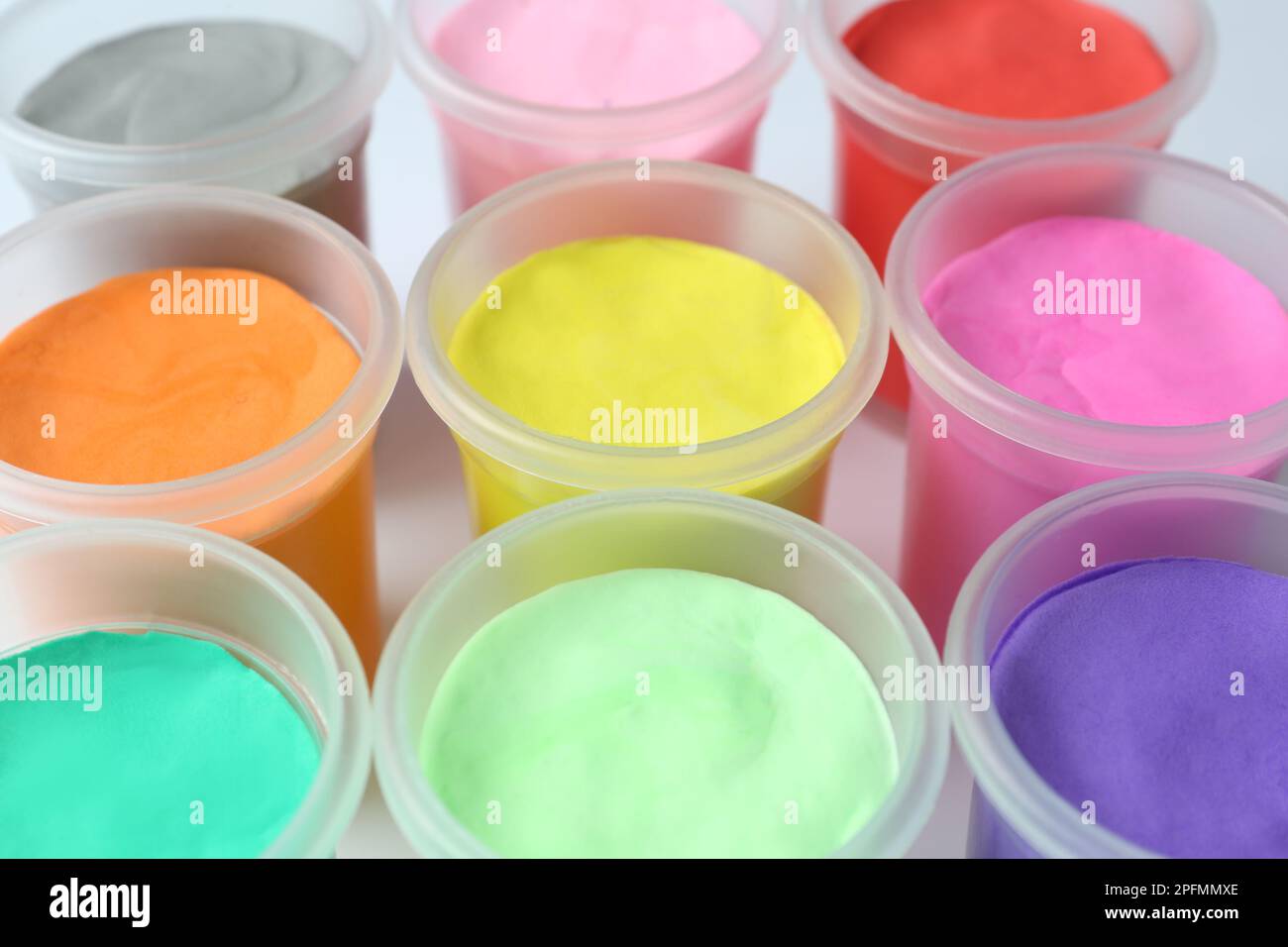 Plastic containers with colorful play dough on white background ...