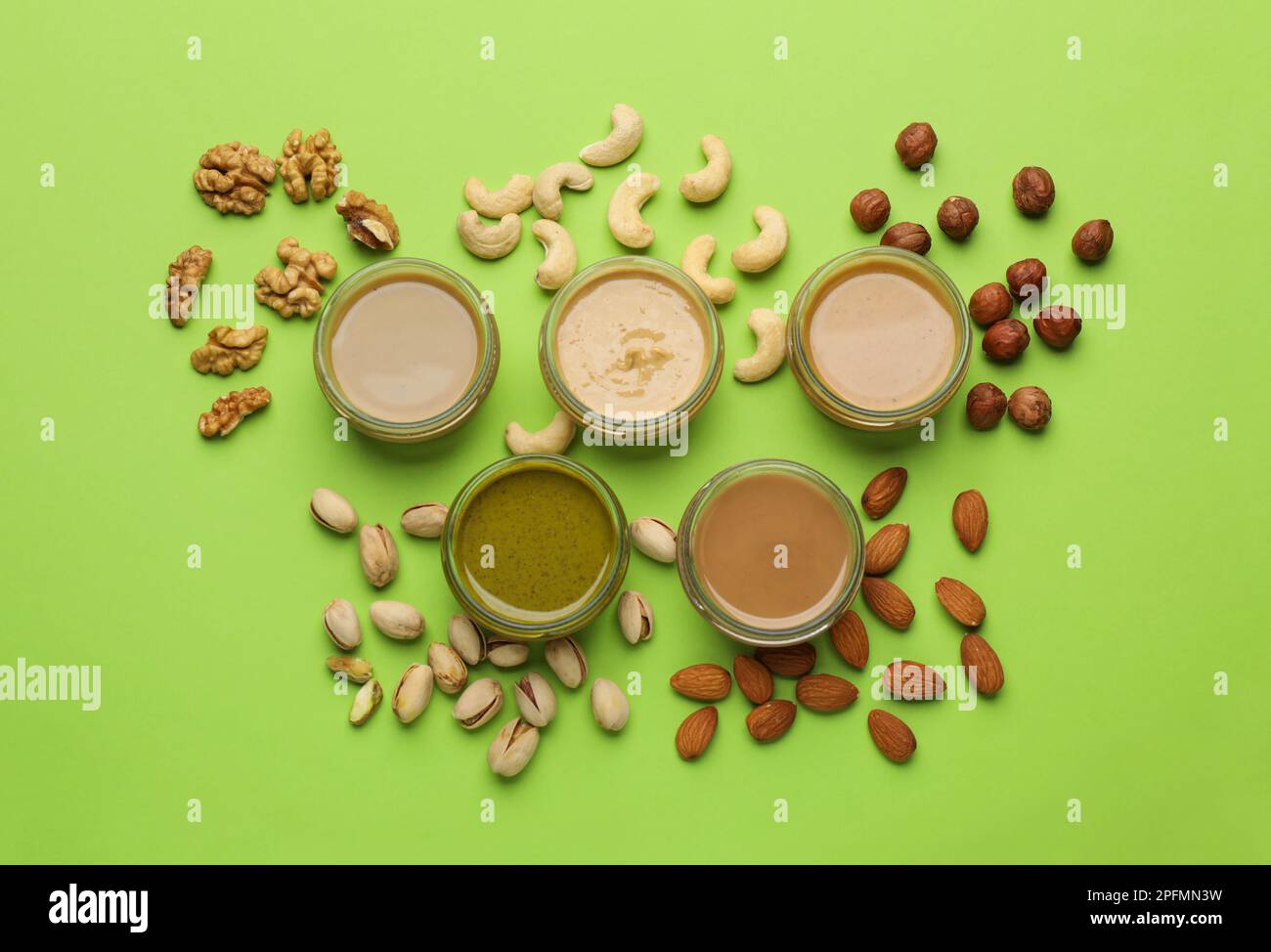 Different types of delicious nut butters and ingredients on light green ...