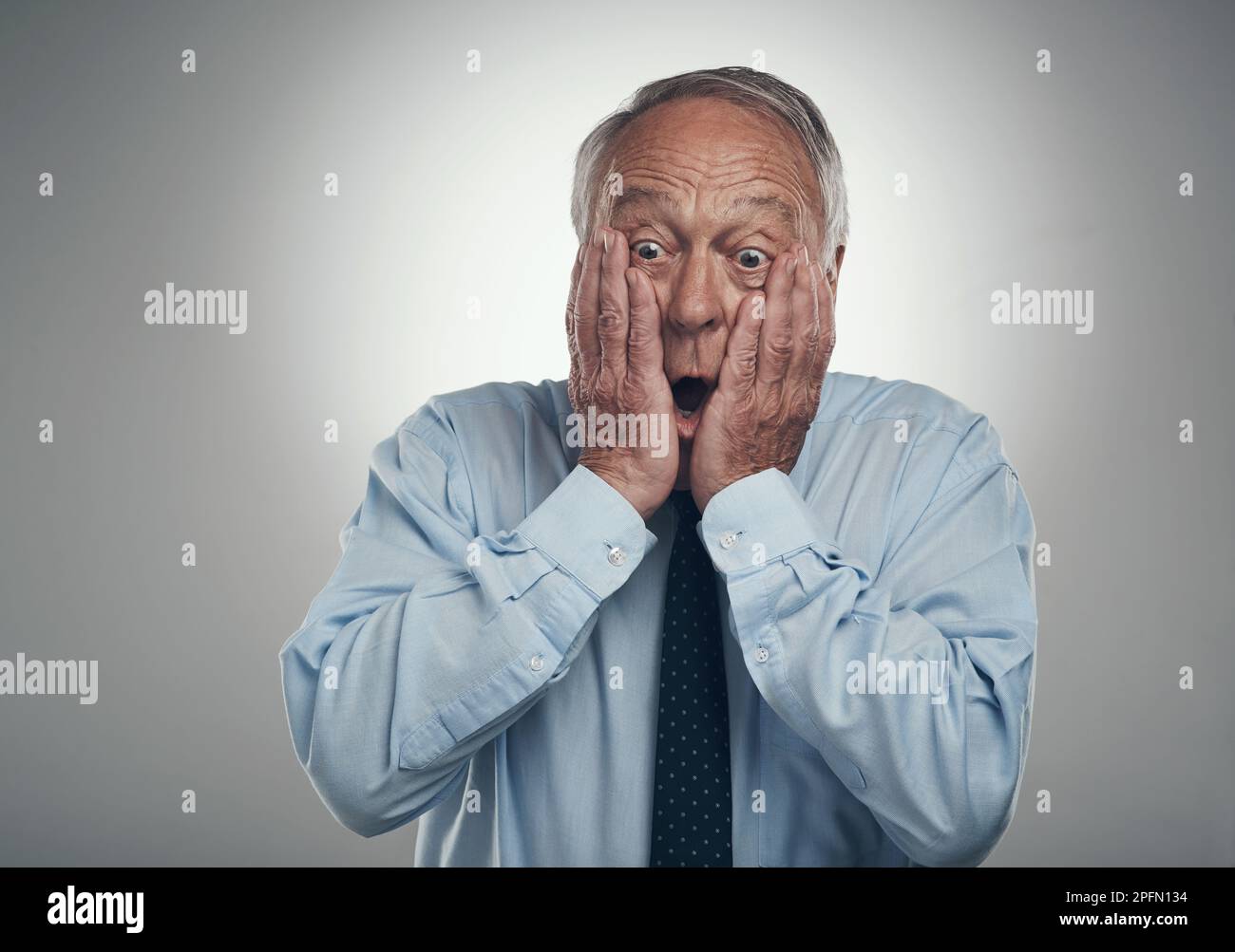 Oh my goodness. a senior businessman standing against a grey studio ...