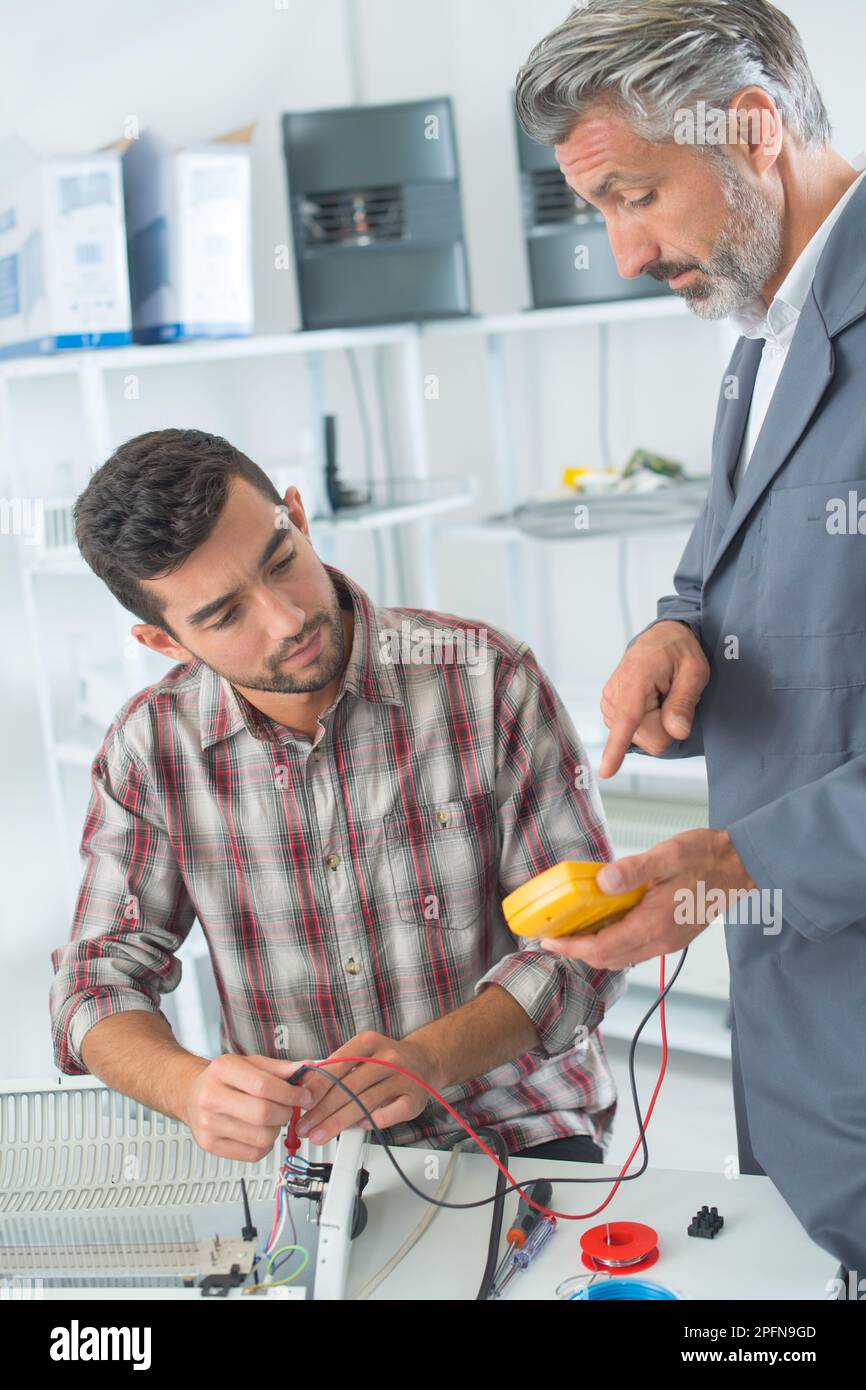 supervisor instructing apprentice using multimeter on electrical ...