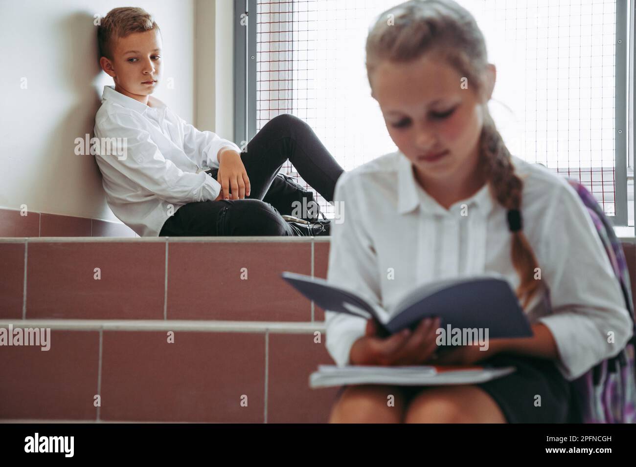 Sad lonely boy sitting on a school stairs next to a girl reading a book ...