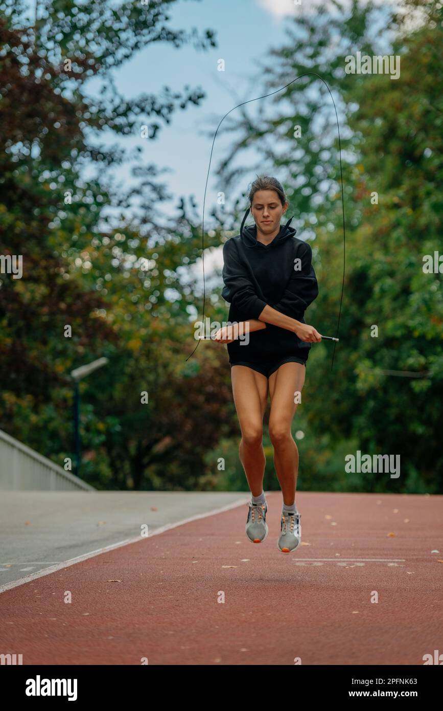 A cute young female athlete with muscular legs is jumping rope on a red ...