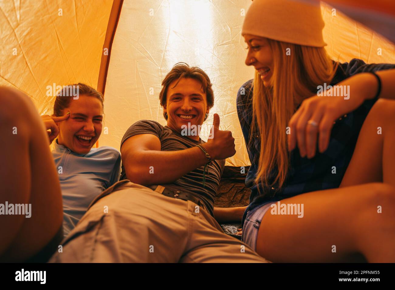 Three friends having fun and laughing while laying at the orange tent ...