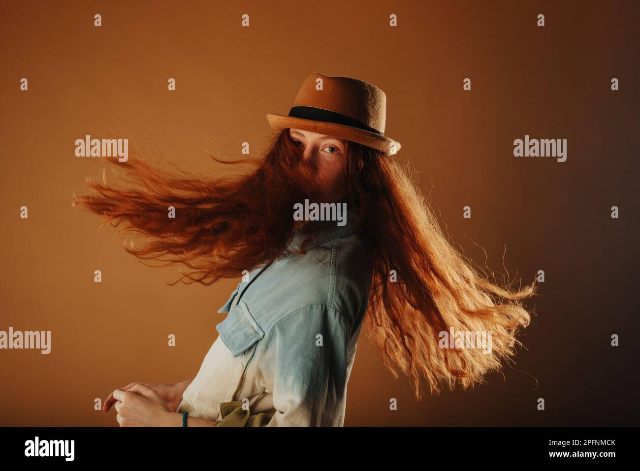 Cute red head fliping her hair while standing at the studio on a orange ...