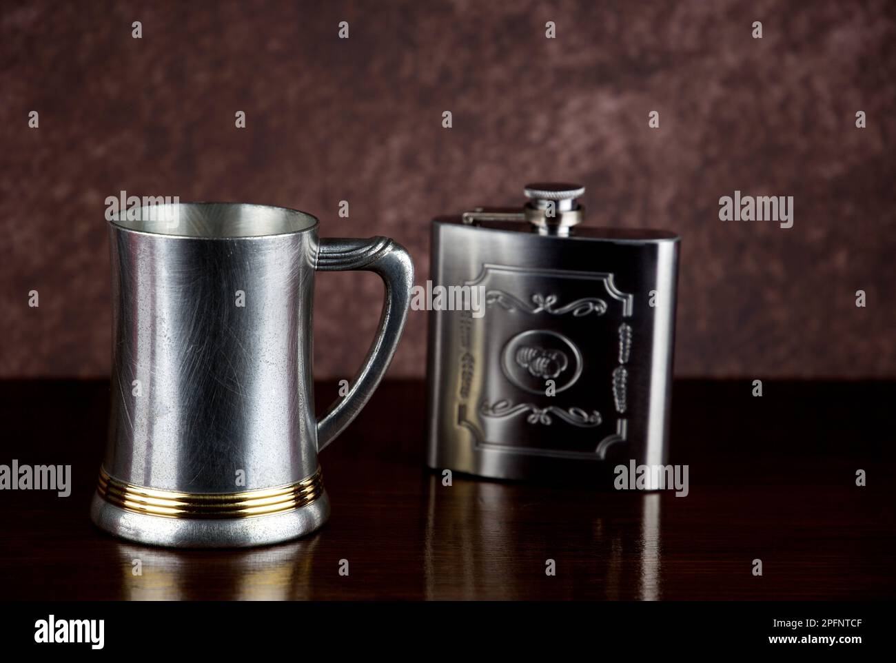 Old pewter drinking tankard and stainless steel hip flask on a polished ...