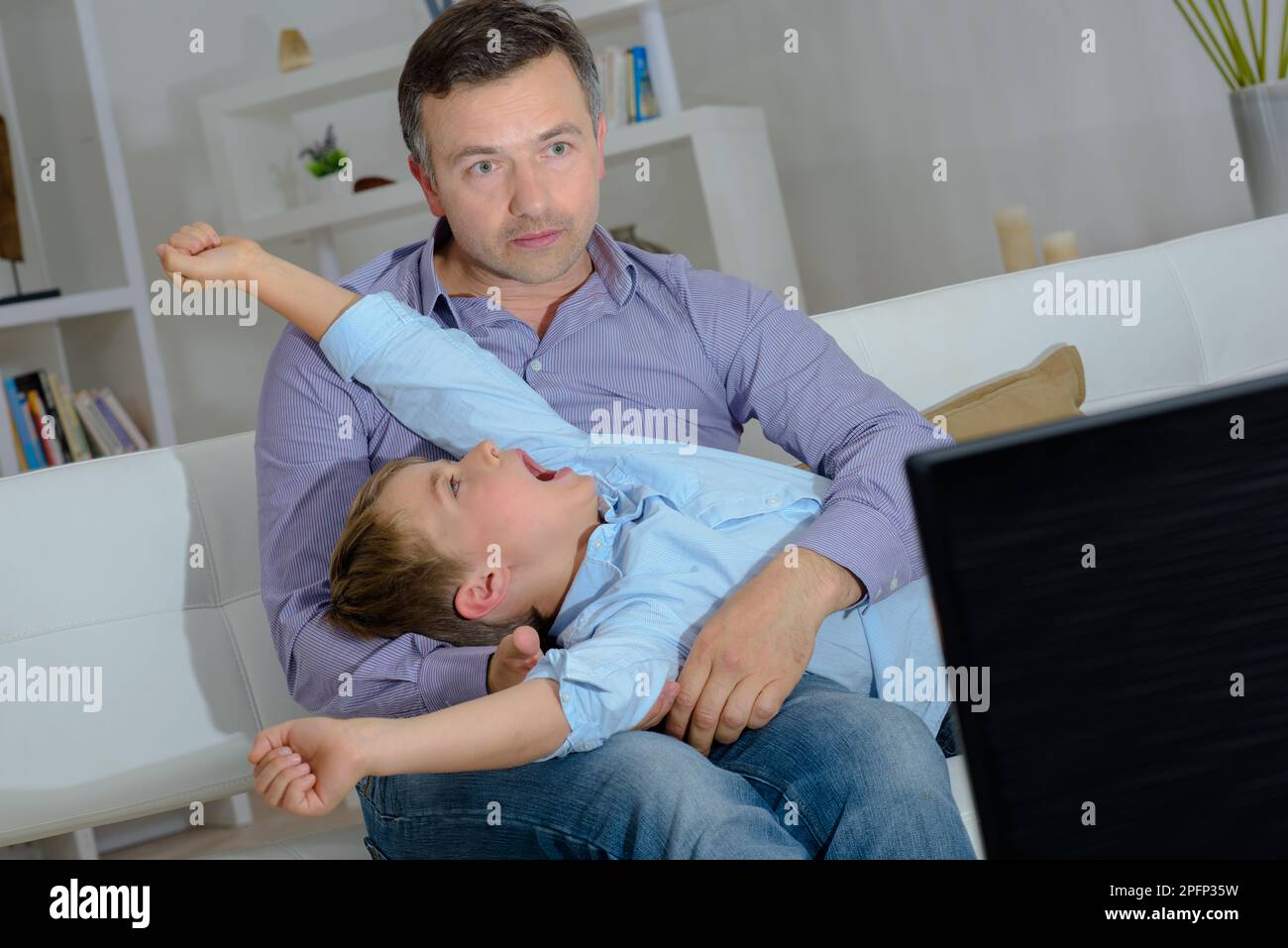 Man watching television, child layed across his lap yawning Stock Photo ...