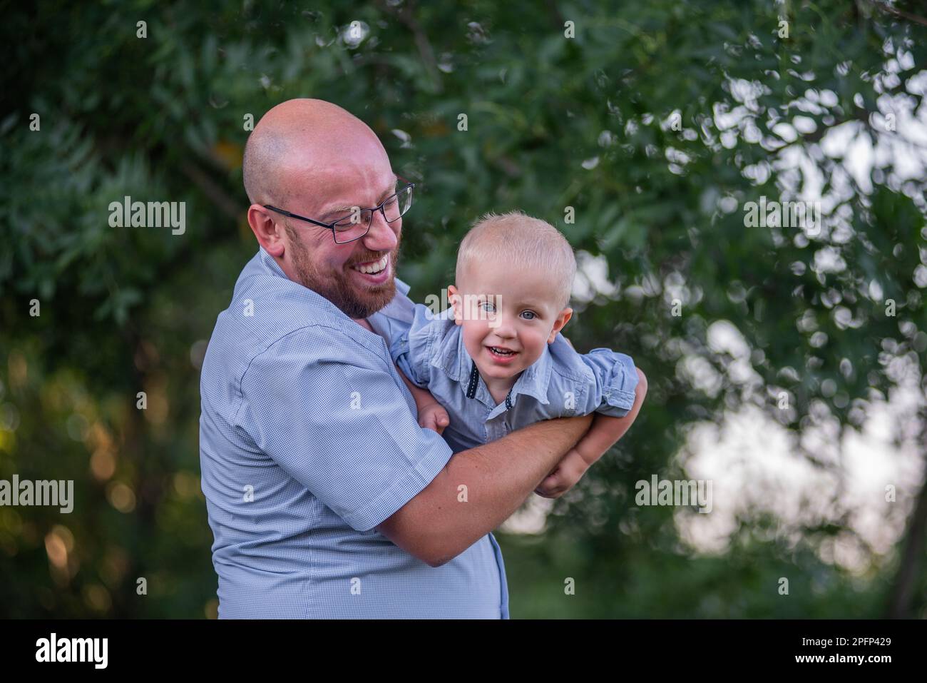 Bald man with glasses throws child into the sky air. Father in jeans ...
