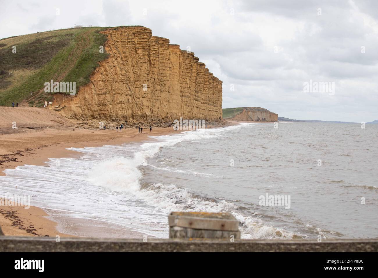 People walk under the very high and steep sand formation cliffs in West ...