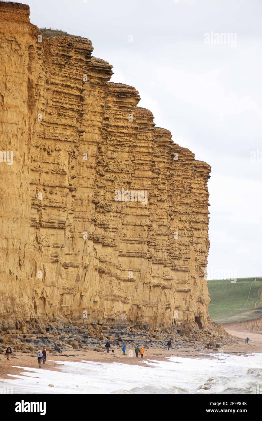 People walk under the very high and steep sand formation cliffs in West ...
