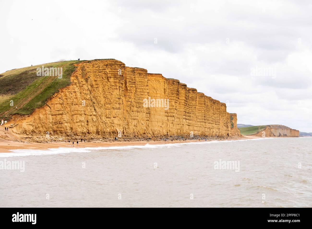 People walk under the very high and steep sand formation cliffs in West ...