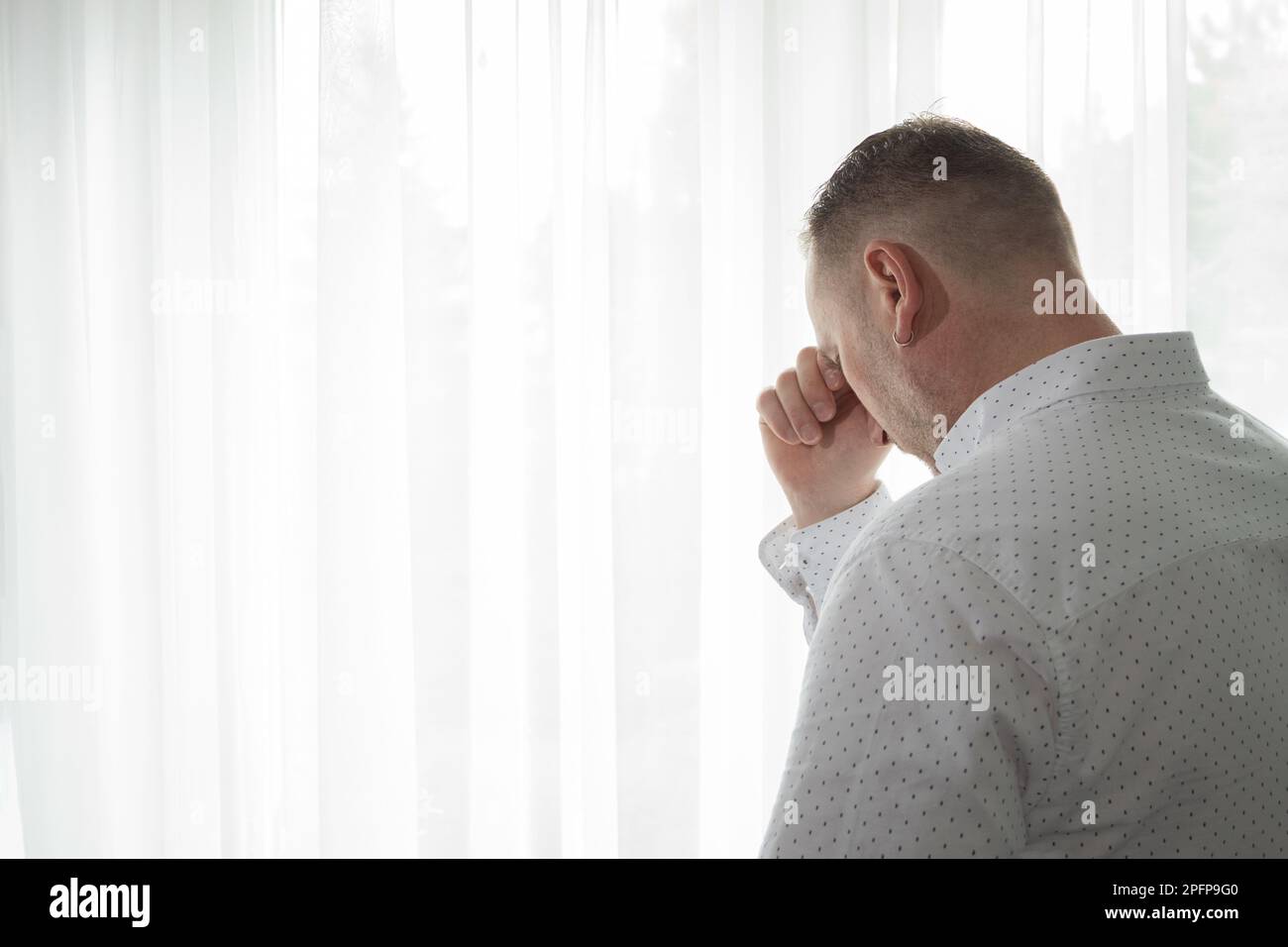 A modern man mourns while standing at the window. A man is experiencing ...