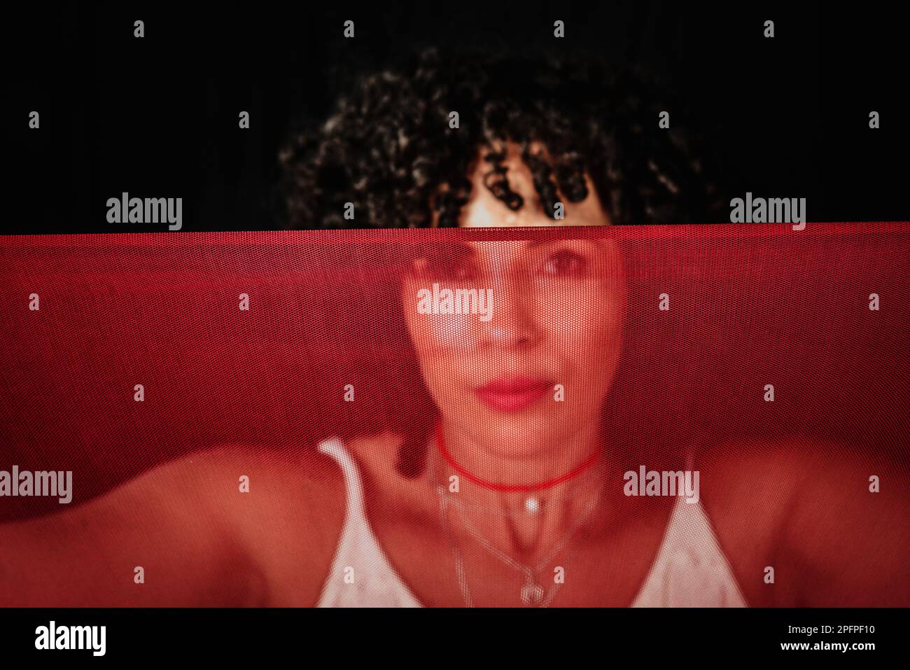 Portrait of a woman with red cloth stretched in front of her face ...