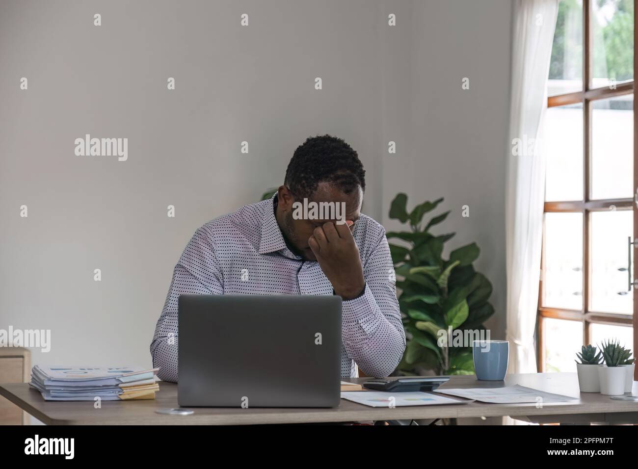 Stressed business man sitting at office workplace. Tired and overworked black man. Young african ...