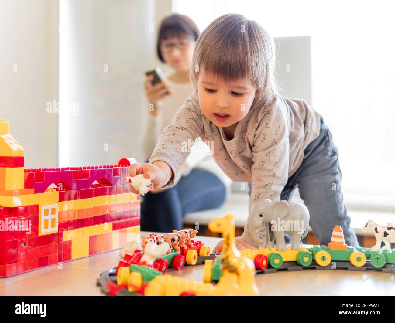 Toddler plays with colorful toy blocks while his mother or babysitter ...